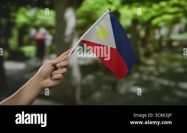 Male hand holding a philippine flag outdoors in a park, capturing a ...