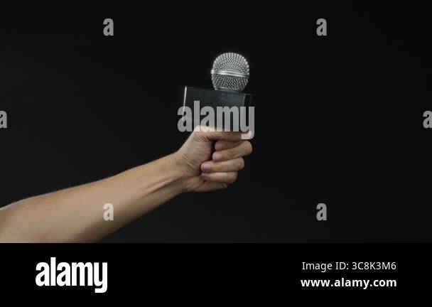 Man holding microphone against black background with hand raised for ...