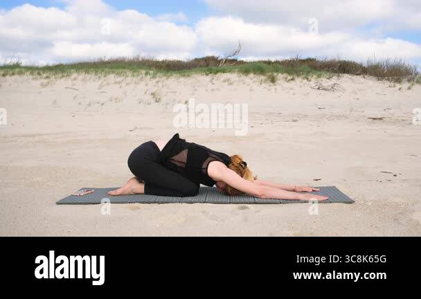Woman practicing childs pose yoga or Balasana on sandy beach at sunrise ...