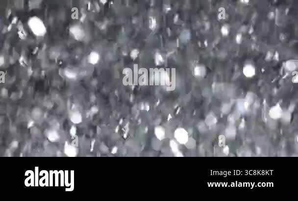 Numerous silver and white glitter particles in swirling motion on dark ...