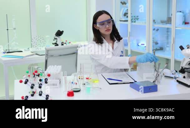 Female scientist with goggles arranges equipment on sterile workplace ...