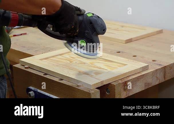 Carpenter sanding a wooden door on a workbench in a carpentry workshop ...