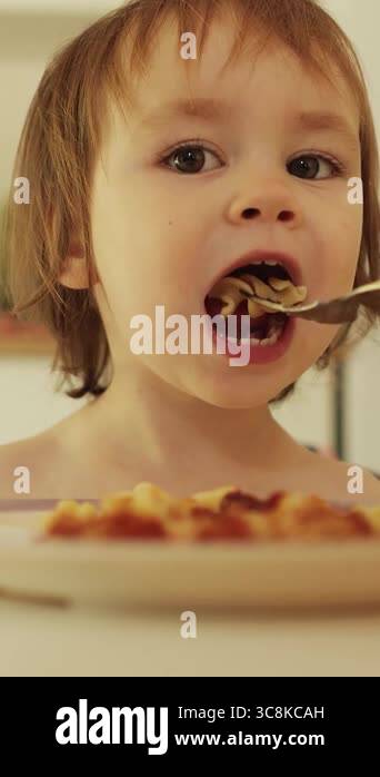 Vertical video. Toddler happily eats pasta in a cozy and bright white ...