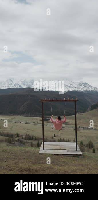 A girl tourist swings on a swing on a mountain cliff and enjoys the ...