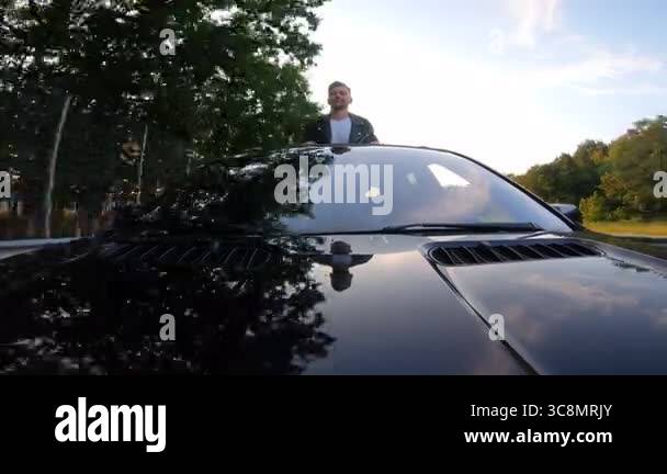Handsome funny man standing out of car sunroof and raising hands ...