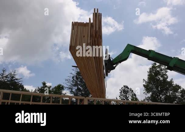 Forklift telehandler crane lifts large wooden truss into place, helping ...