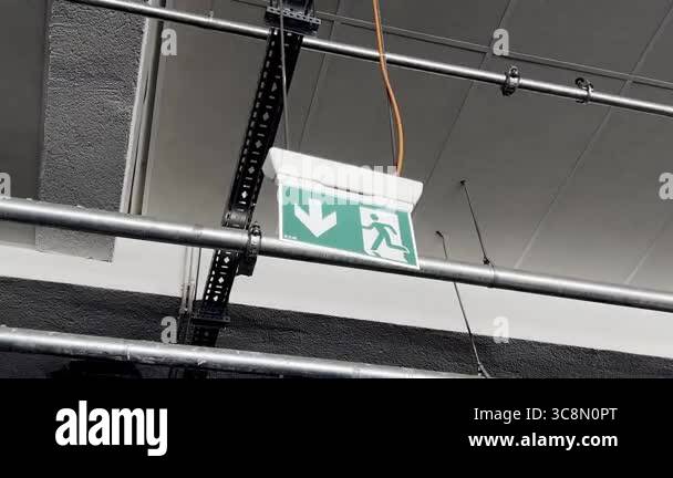 Green fire exit sign hanging from ceiling, illuminated guidance system ...