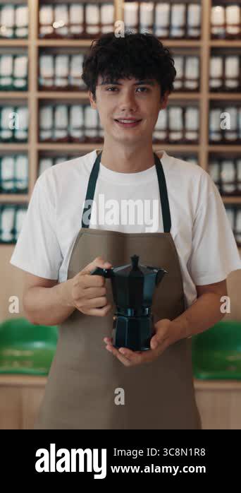 Portrait of young man waiter in uniform holding geyser coffee maker ...