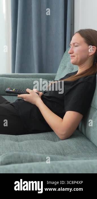 The young woman sat comfortably on the sofa, watching TV, changing ...