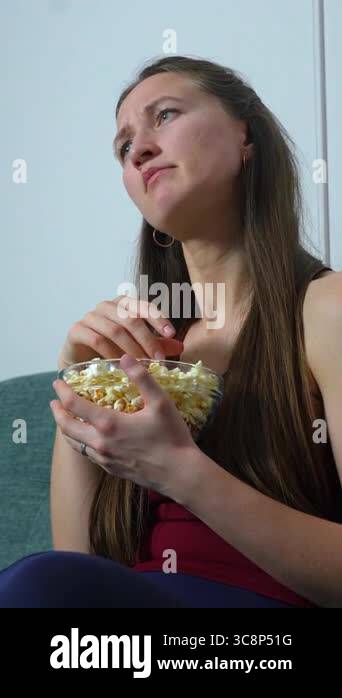 Young woman sitting on green sofa, holding a bowl of popcorn in her ...