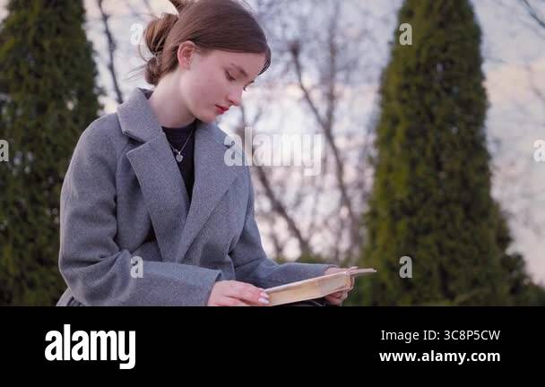 Student girl teenager relaxing on park bench, reading book and drinking ...