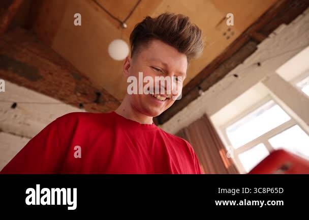 Young man in red t-shirt looks down, texting on smartphone, and smiles ...