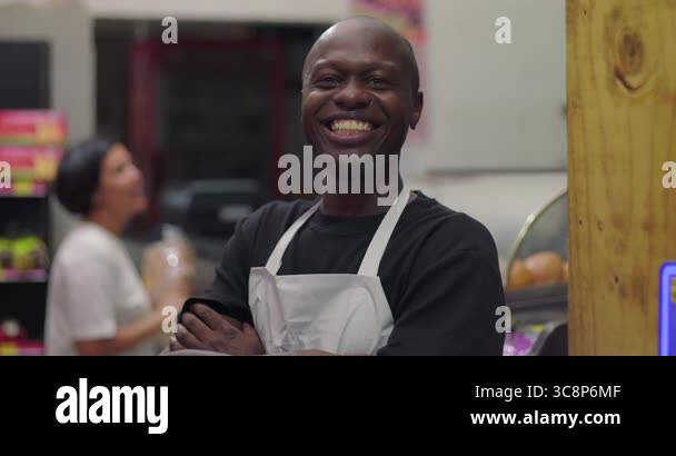 Smiling African American deli worker in apron standing confidently with ...