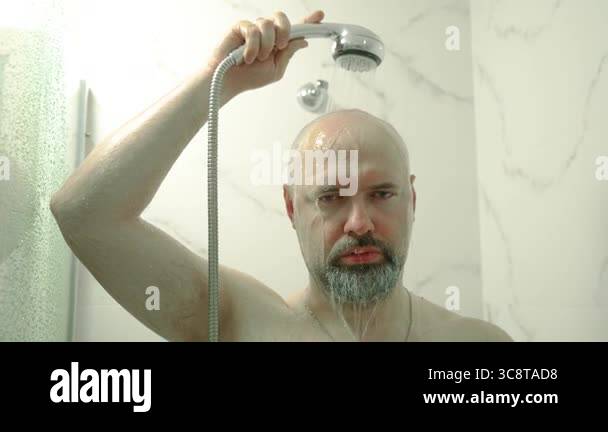 Indifferent sad man pouring water over head in shower and sighing ...