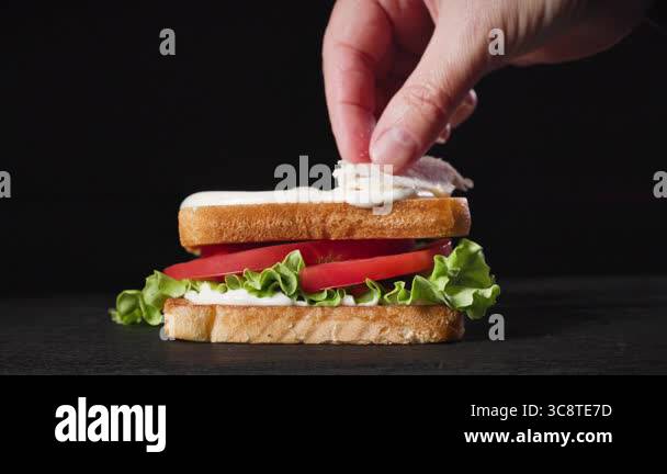 A cook put chicken meat on fresh toasted bread slice on black wooden ...