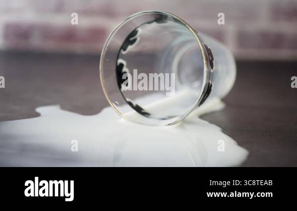 A glass lies overturned while milk spreads across the table surface ...