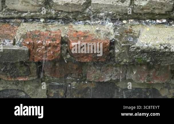 Close-up of heavy rain falling on brown brick wall of an old, partially ...