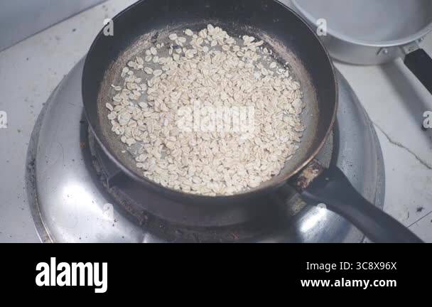 Pouring oats into a black pan placed on a gas stove, ready for cooking ...