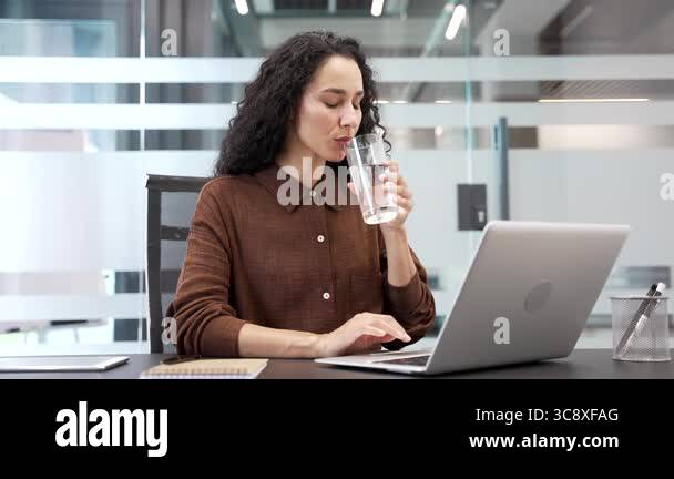 Young businesswoman drinks water from a glass while sitting at desk at ...