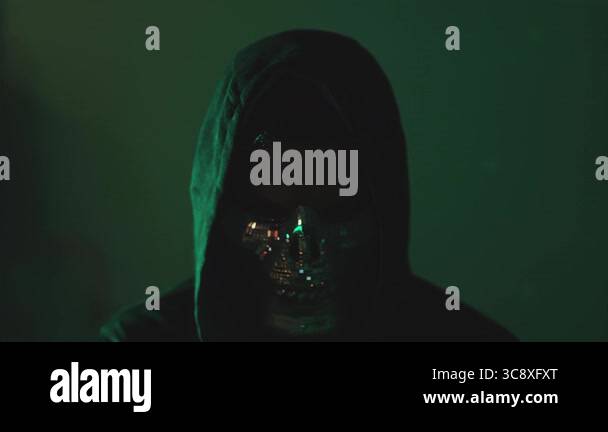 Suspicious figure in dark room watching camera in hoodie and mask ...