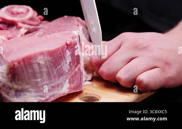 A butcher removes the fascia from a beef steak with a large knife in a ...