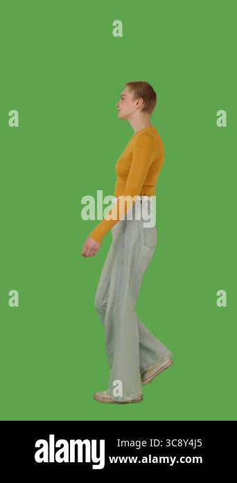 A person in a yellow sweater and wide leg jeans walks on green screen ...