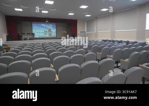 Large auditorium contains rows of fabric seats facing stage with ...