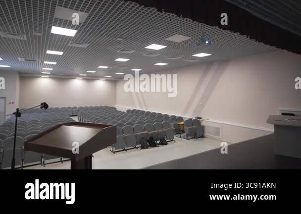 Stage with dark podium overlooks neat rows of gray chairs. Grid ceiling ...