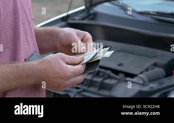 Counting dollars cash for car repair payment near the open hood. A ...