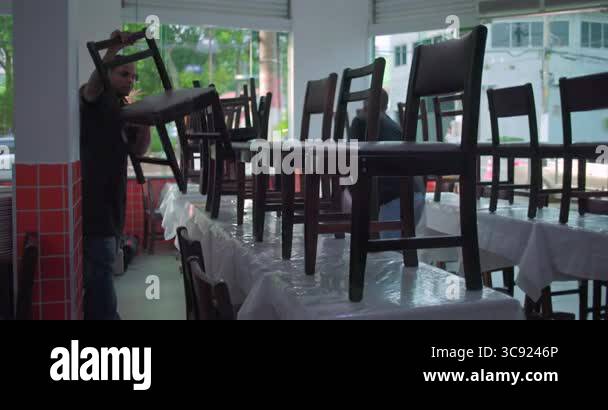 Restaurant workers placing chairs upside down on tables to close for ...