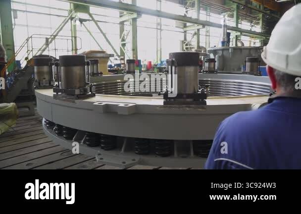 Factory worker inspecting a large circular industrial part and taking ...