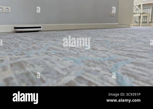 Low-angle view of a robot vacuum cleaner moving across a carpeted floor ...