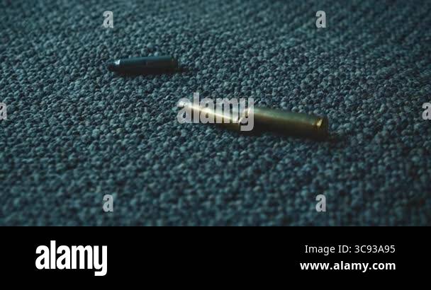 Spent bullet casings fall and scatter across a textured carpeted floor ...