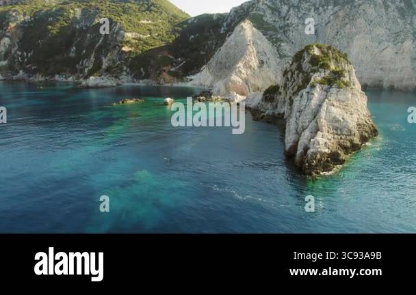 Sharp rocky cliffs and clear blue sea waters in a secluded green cove ...
