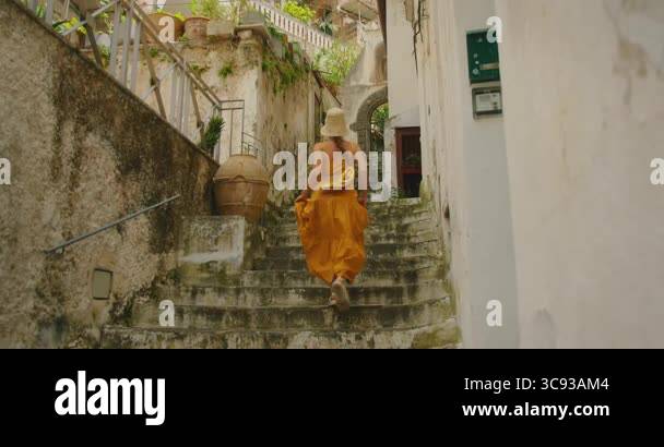 Back view of woman in dress easily climbs up stone steps in narrow ...
