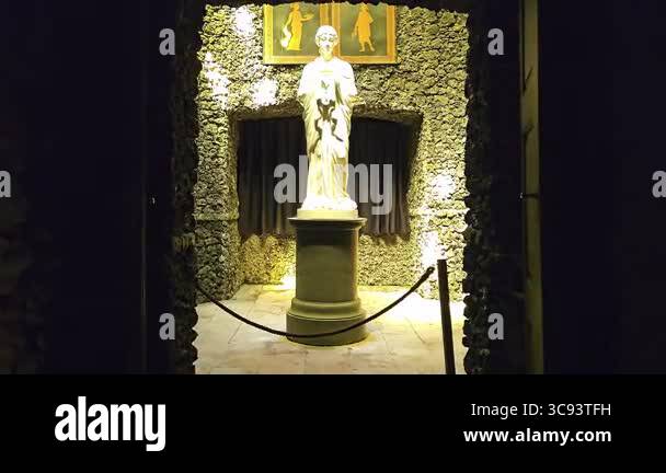 A white statue, set on a pedestal in a softly lit stone-walled grotto ...