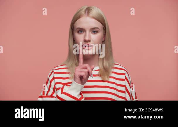 Serious young woman in striped sweater making shhh gesture, holding ...