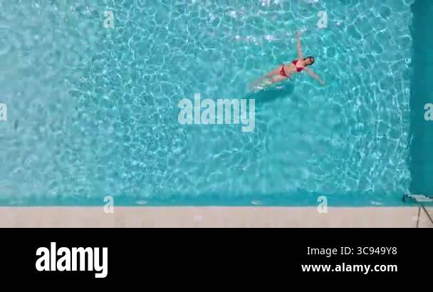Top down view of a woman in red swimsuit lying on her back in the pool ...