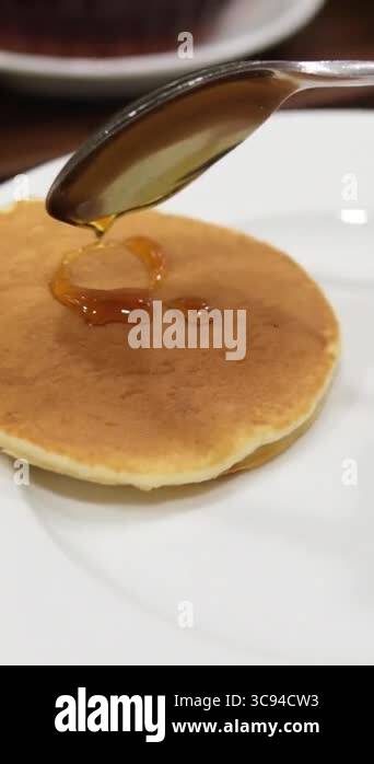 Generous dollop of maple syrup or honey falls from spoon onto plate of ...