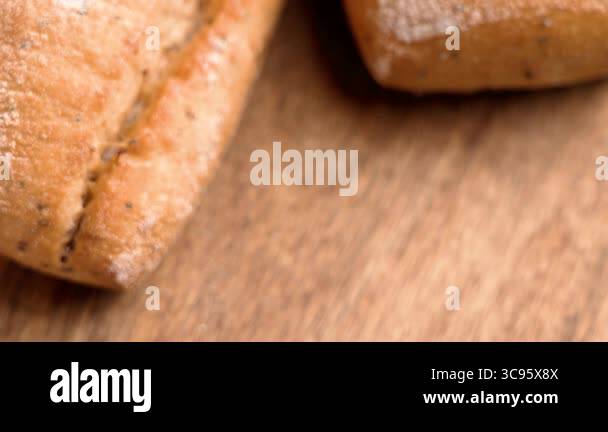 Hand placing fresh toasted bread roll on rustic wooden table. Macro ...