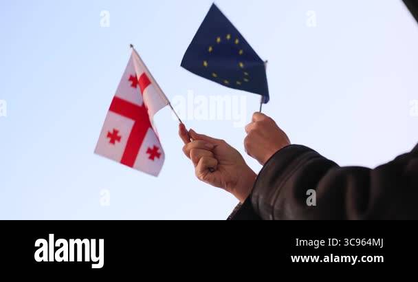 Person waves Georgian and European Union flags during outdoor political ...