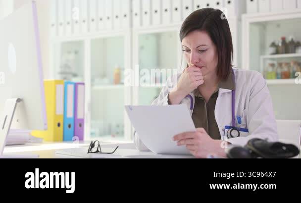 Female doctor reads patient medical records shaking head at workplace ...