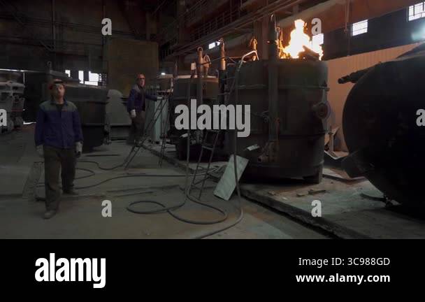 Industrial workers operate a furnace in a metal foundry, showcasing the ...