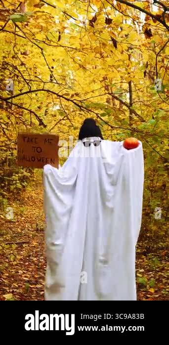 Man wearing ghost costume dancing holding cardboard with text TAKE ME ...