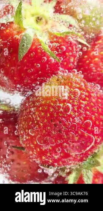 Ripe strawberries in sparkling water close-up. Bubbles in water and ...