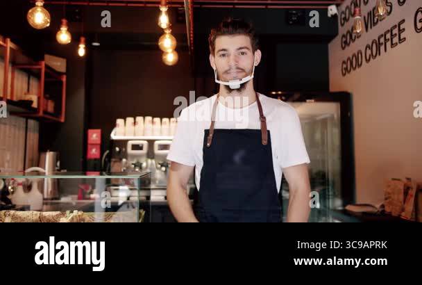 Positive young male barista smiling and looking at camera while ...