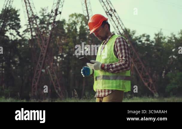 Engineer inspects high-voltage power lines, using tablet for ...