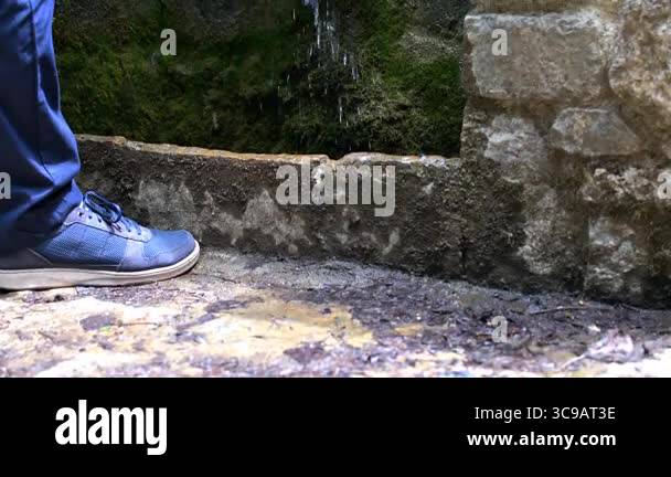 A person is washing his hands at a rock made spring in the forest. Tilt ...