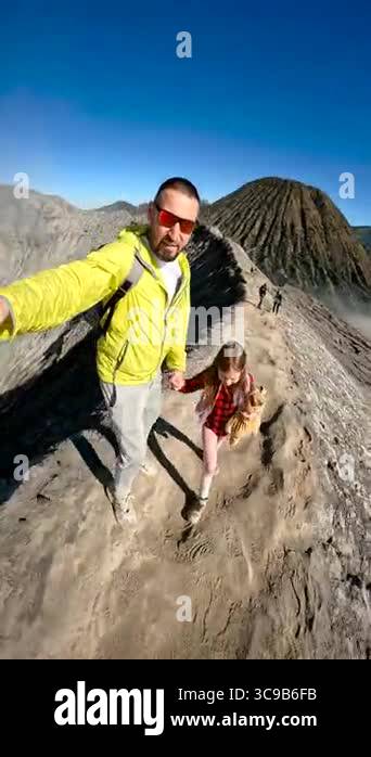 A man and young girl walk along the dusty crater ridge of an active ...