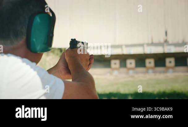 Older man with ear protection aiming a handgun at shooting range ...